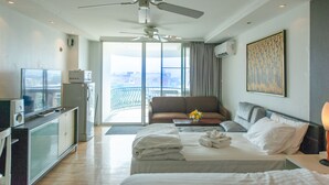 Quarto de hotel com cama, sofá, televisão, ventoinha no teto e vista para a cidade.