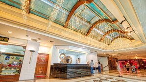Um saguão de hotel com piso xadrez, um balcão de recepção e um teto com luminárias pendentes.