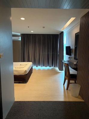 Quarto de hotel com cama, escrivaninha, cadeira e televisão.