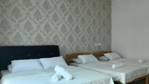 Quarto de hotel com duas camas, cada uma com roupa de cama e almofadas brancas, cabeceira escura e papel de parede estampado.