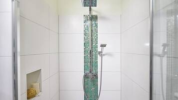 Área de chuveiro com parede revestida em azulejos verdes, chuveiro manual e box de vidro.