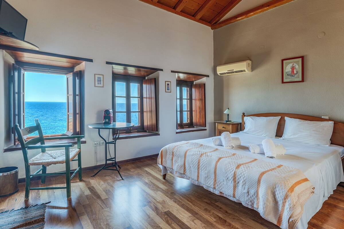 Quarto com uma cama grande, escrivaninha e cadeira perto de uma janela com vista para o mar.