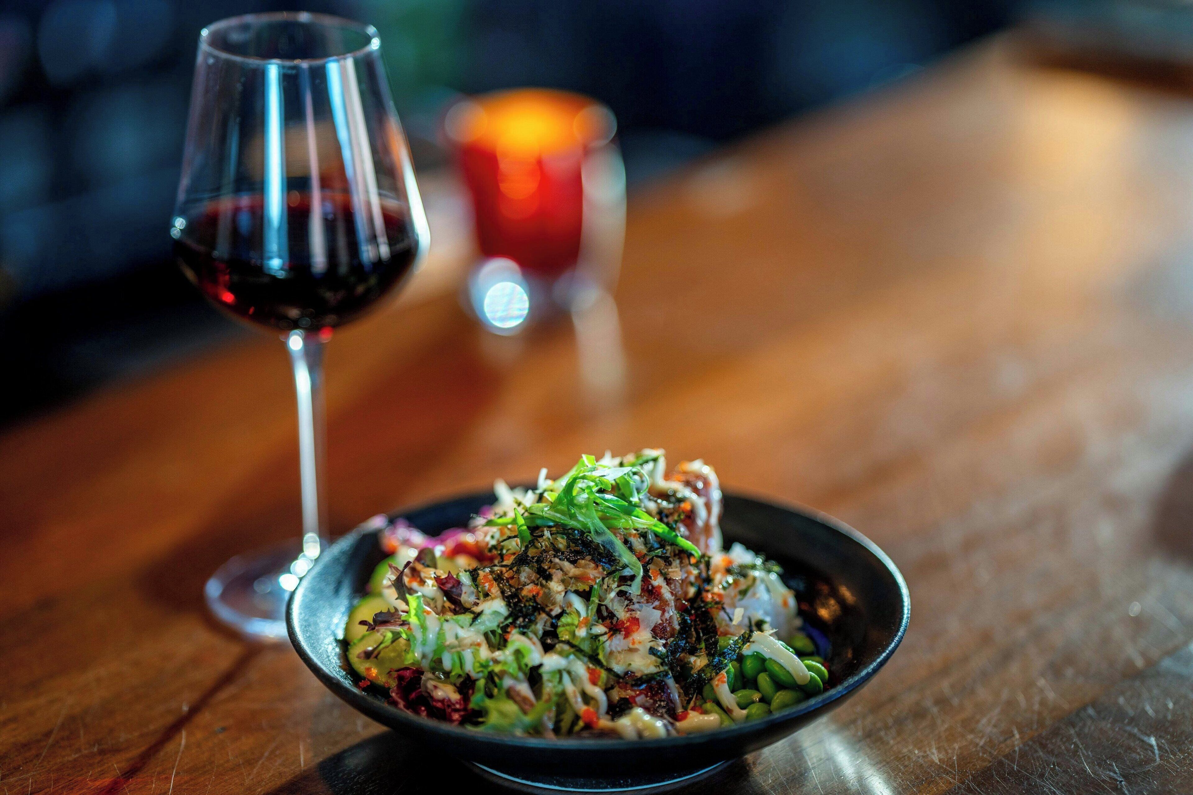 Uma tigela de comida com um copo de vinho tinto sobre uma mesa de madeira.