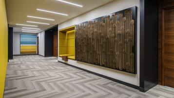 Um corredor moderno com carpete estampado, um espaço de estar amarelo e um painel decorativo na parede.