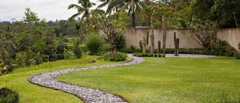 Um jardim com um caminho de cascalho sinuoso, palmeiras e um muro de concreto.