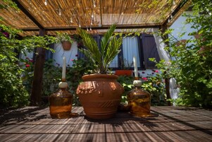Um vaso de terracota com uma planta e duas garrafas sobre uma mesa de madeira sob um telhado de bambu.
