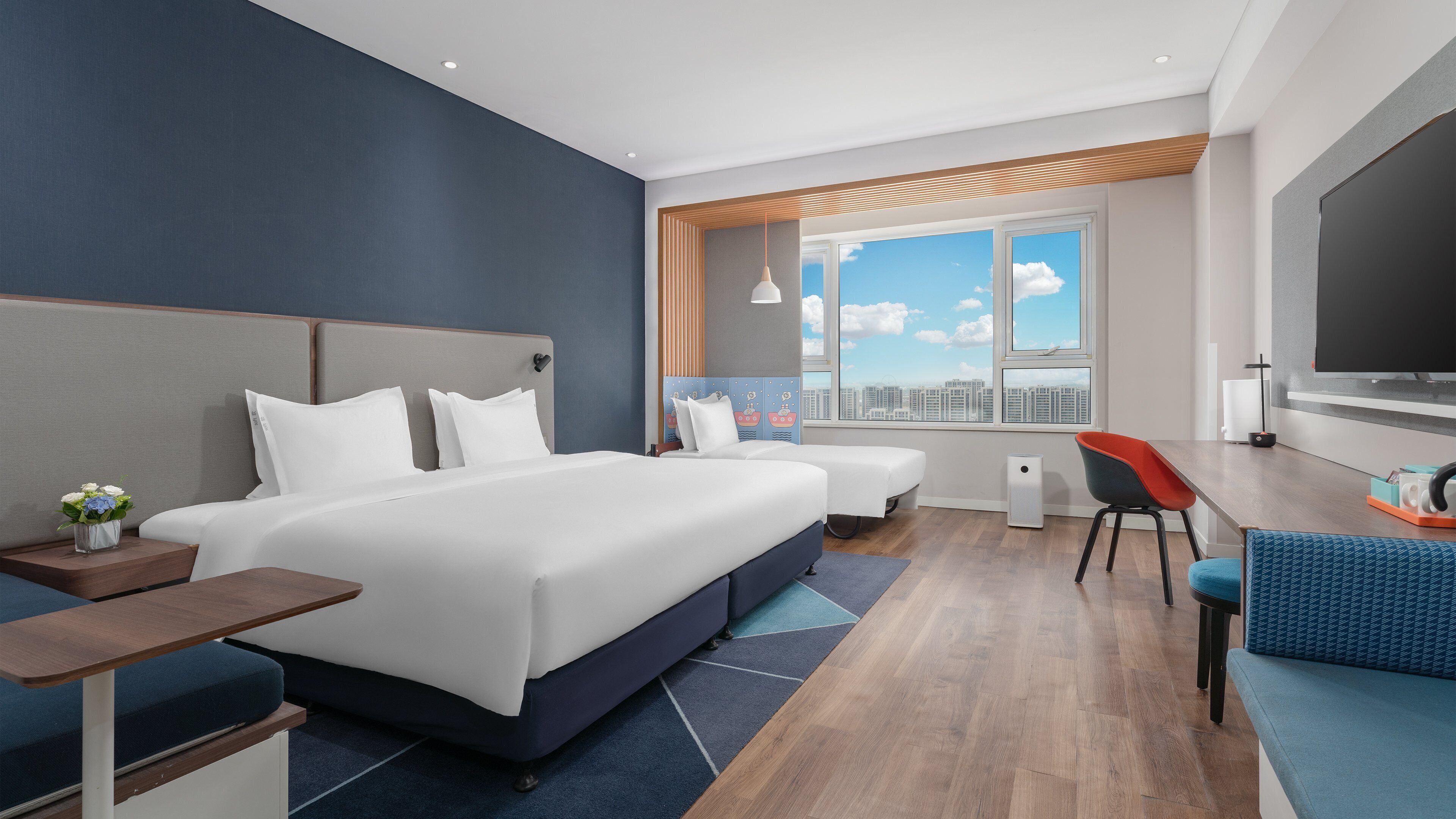 Quarto de hotel moderno com uma cama grande, área de estar, televisão e vista para a cidade.