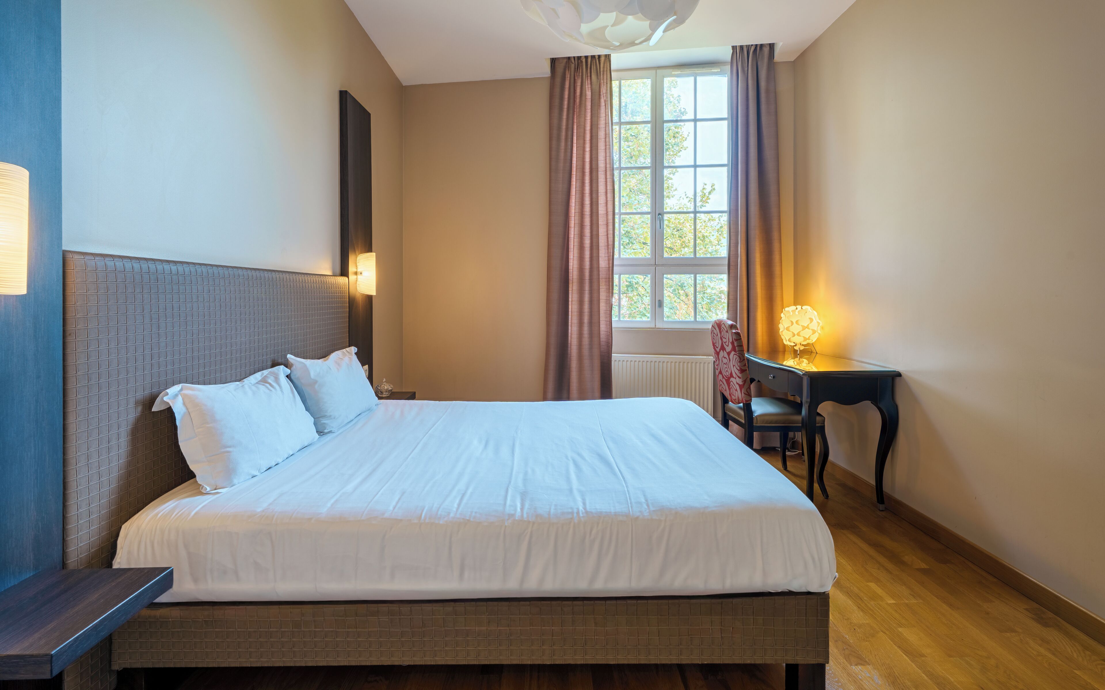 Quarto de hotel com uma cama grande, uma escrivaninha e uma janela com cortinas.