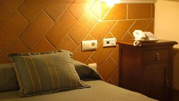 Quarto de hotel com cama, mesa de cabeceira com telefone, tomada e luminária na parede.