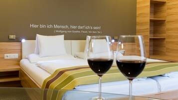 Quarto de hotel com uma cama, dois copos de vinho e uma frase na parede.