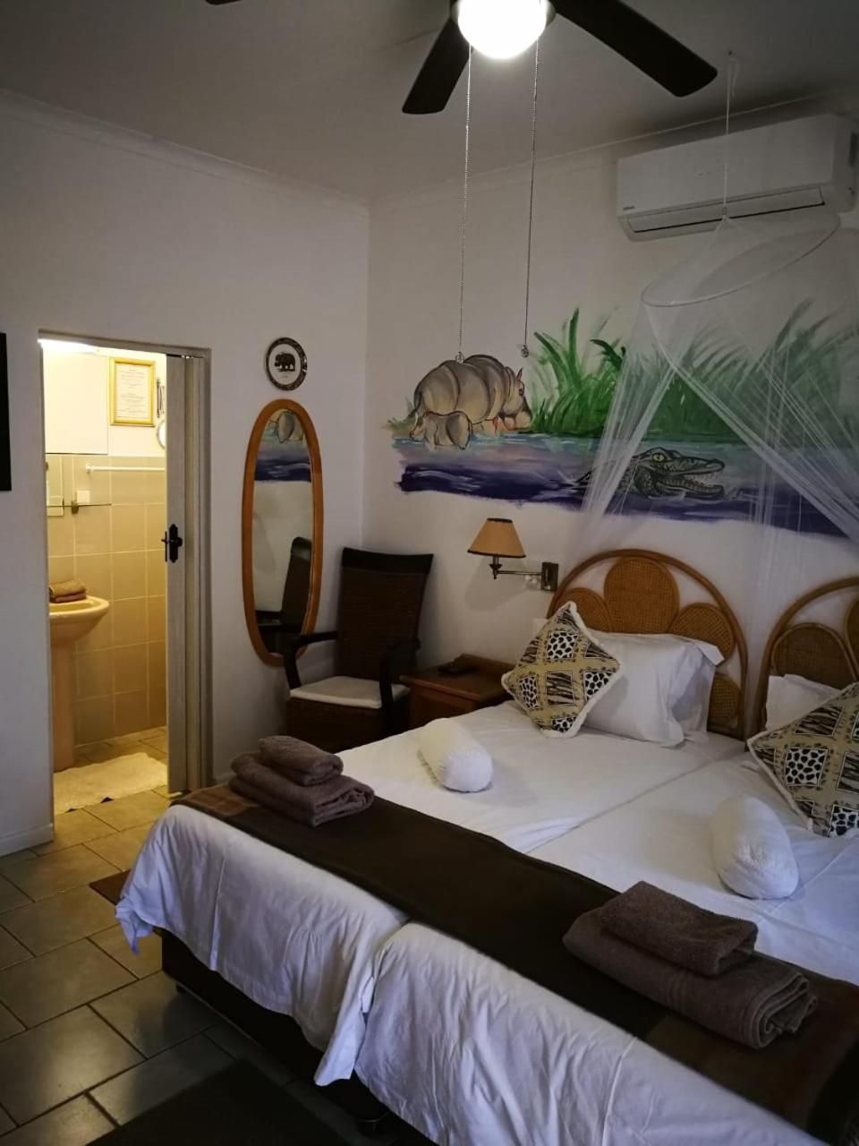 Quarto de hotel com cama, cadeira, mesa de cabeceira, espelho e parede com um mural.