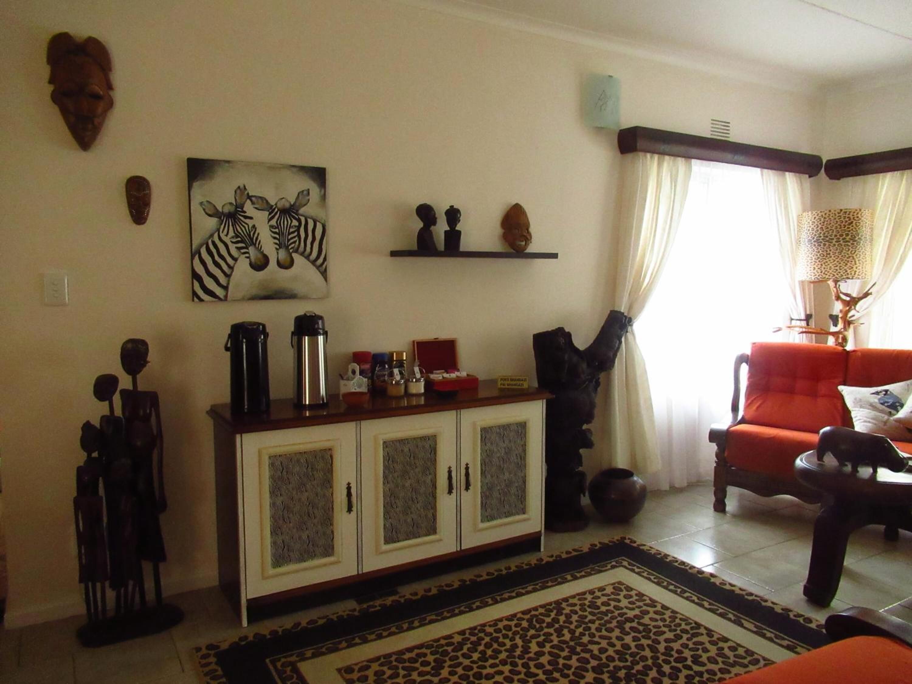 Uma sala de estar com um sofá, um aparador com objetos decorativos, uma pintura de zebra e um tapete com estampa de leopardo.