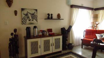Uma sala de estar com um sofá, um aparador com objetos decorativos, uma pintura de zebra e um tapete com estampa de leopardo.