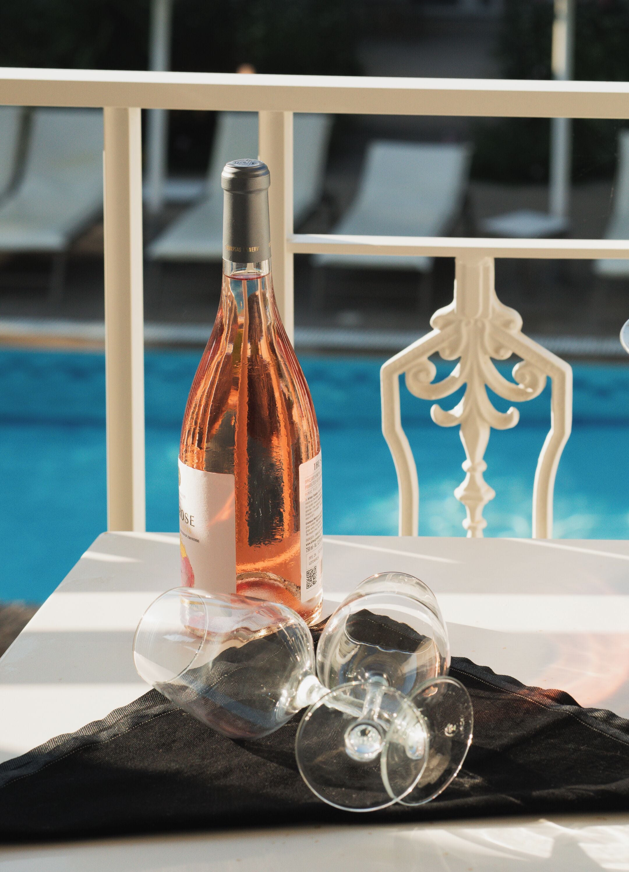 Uma garrafa de vinho rosé e dois copos sobre uma mesa perto de uma cadeira à beira da piscina.