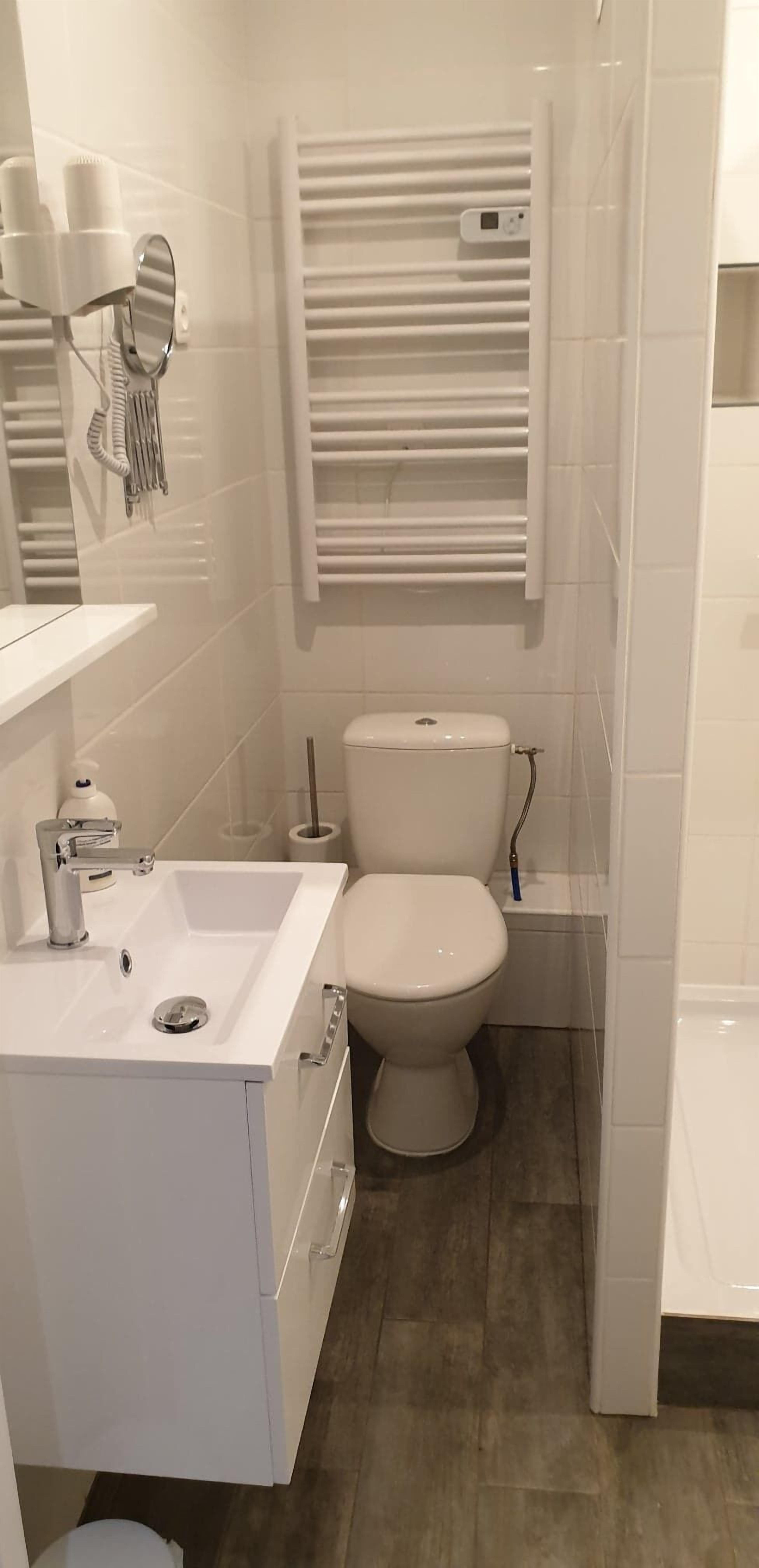 Uma casa de banho pequena e moderna, com uma sanita, uma pia branca e um porta-toalhas sobre a sanita.
