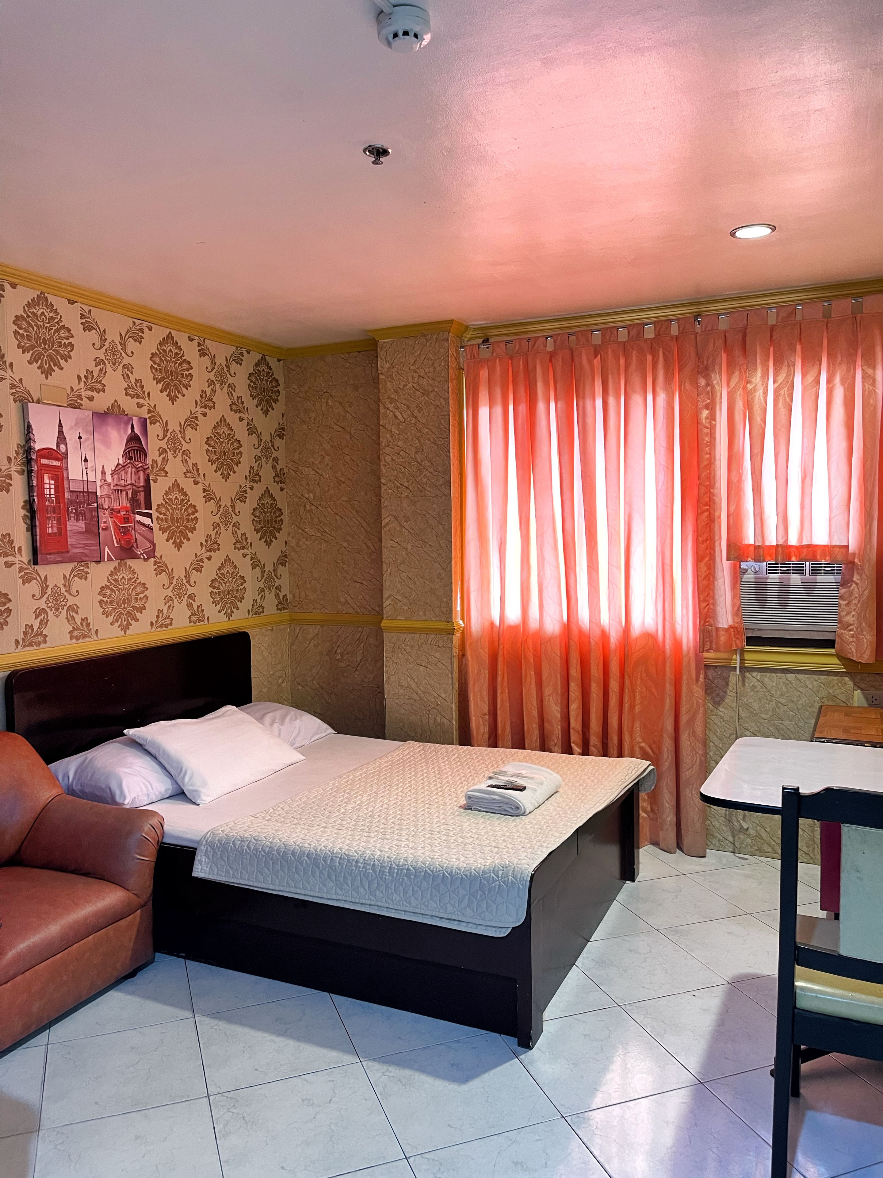 Quarto de hotel com cama, poltrona, mesa, ar-condicionado fixado na parede e luminária no teto.