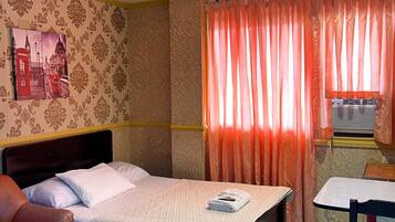 Quarto de hotel com cama, poltrona, mesa, ar-condicionado fixado na parede e luminária no teto.