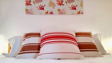 Cama com roupa de cama branca e três almofadas com estampas listradas.