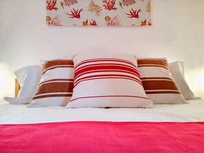 Cama com roupa de cama branca e três almofadas com estampas listradas.
