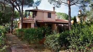 Uma villa em estilo mediterrâneo com um caminho de pedra que leva à entrada, rodeada por vegetação exuberante e árvores altas.