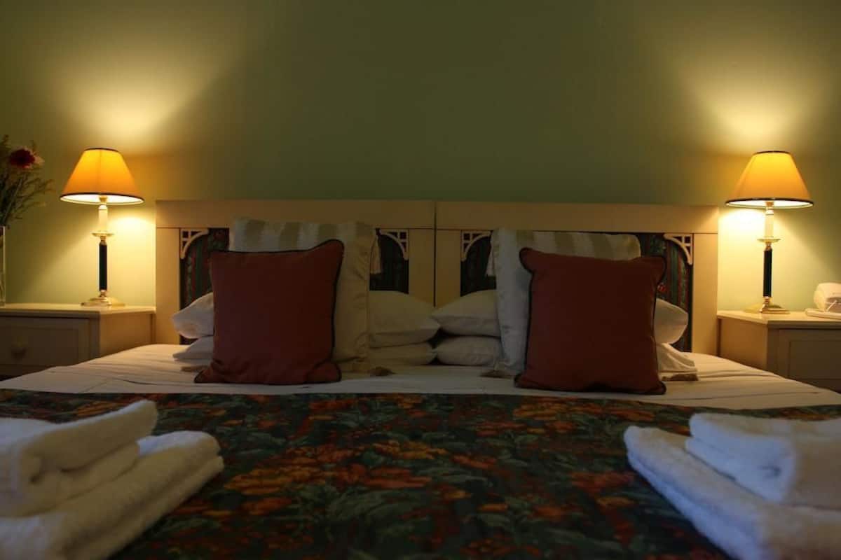 Quarto de hotel com cama, duas mesas de cabeceira, duas luminárias e um cobreleite floral.