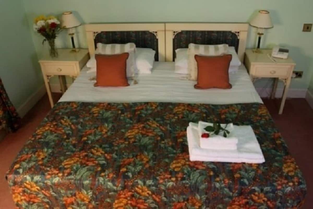Uma cama de casal com roupa de cama florida, duas mesas de cabeceira com abajures e um vaso de flores.