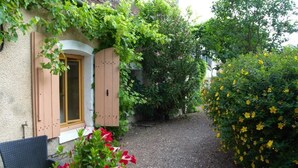 Um jardim com um caminho de cascalho, uma porta de madeira e um banco.