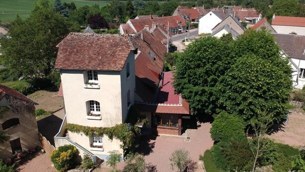 Um edifício em estilo europeu tradicional com telhado de telhas vermelhas, rodeado por vegetação exuberante e um céu claro.