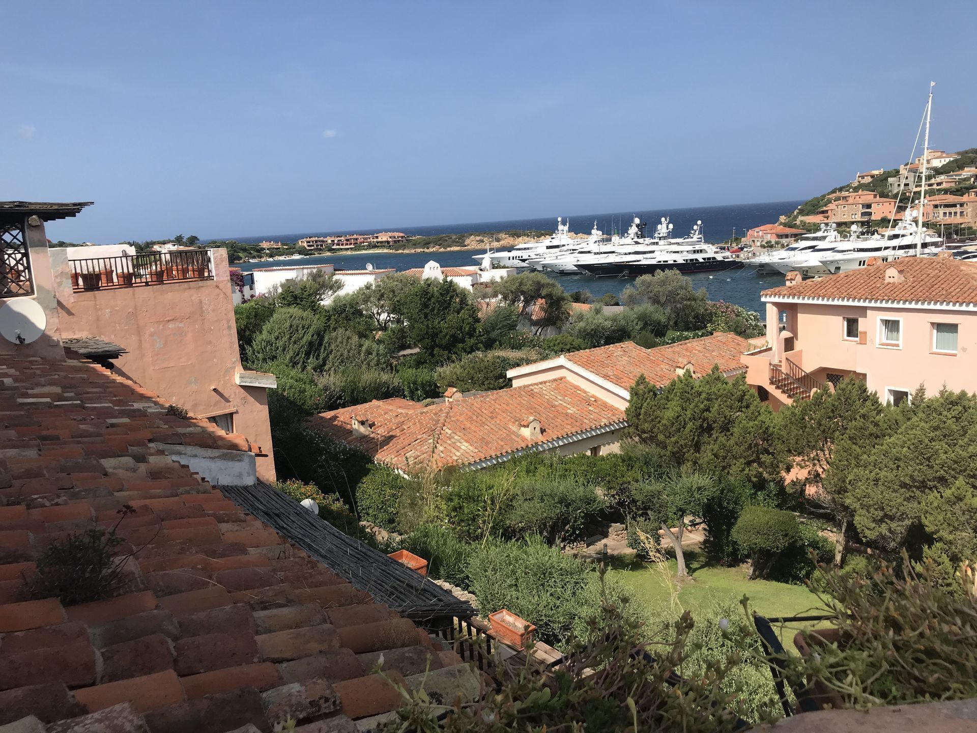 Uma vila costeira com um porto, edifícios com telhados de terracota e vegetação exuberante.