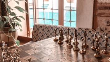 Um tabuleiro de xadrez com peças decorativas em um quarto com uma janela grande e um sofá estampado.