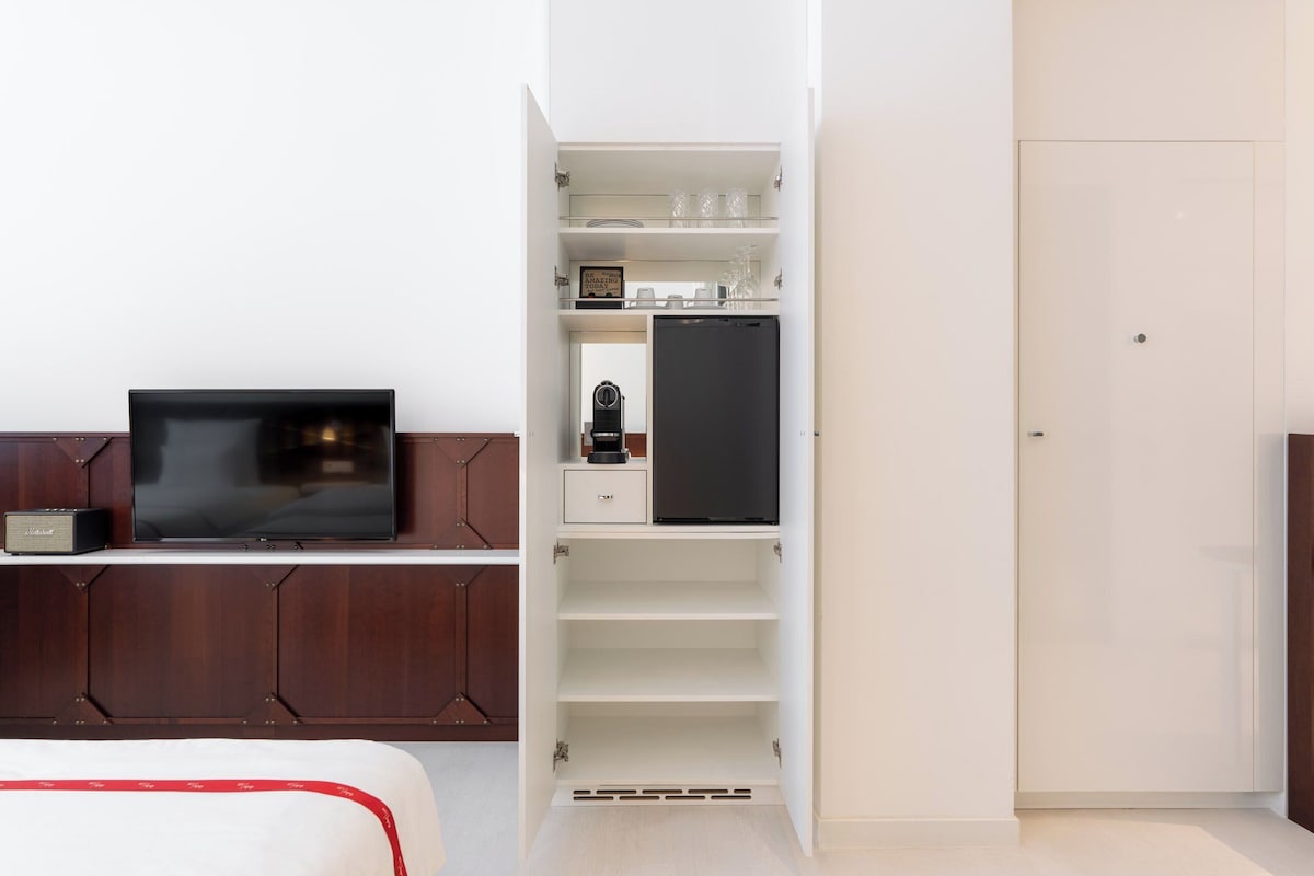 Quarto de hotel com televisão, minibar, roupeiro e uma cama.