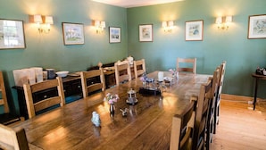 Uma sala de jantar com uma longa mesa de madeira, cadeiras, luminárias fixadas na parede e quadros emoldurados.