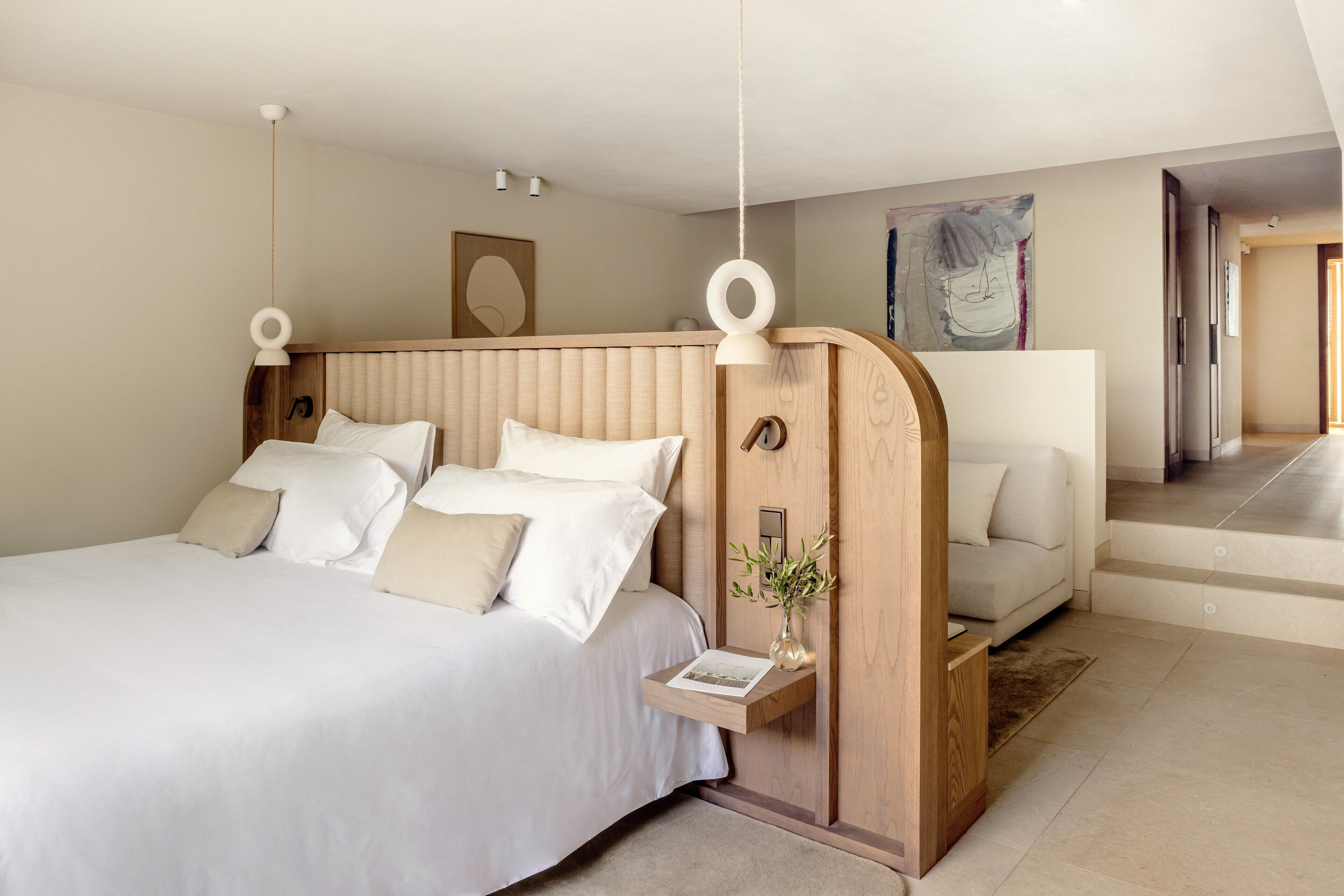 Quarto moderno com uma cama grande, cabeceira de madeira, mesa de cabeceira com um vaso e vista para o corredor.