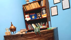 Uma receção com bancada de madeira, uma pequena planta em cima e uma estante cheia de livros e objetos decorativos.