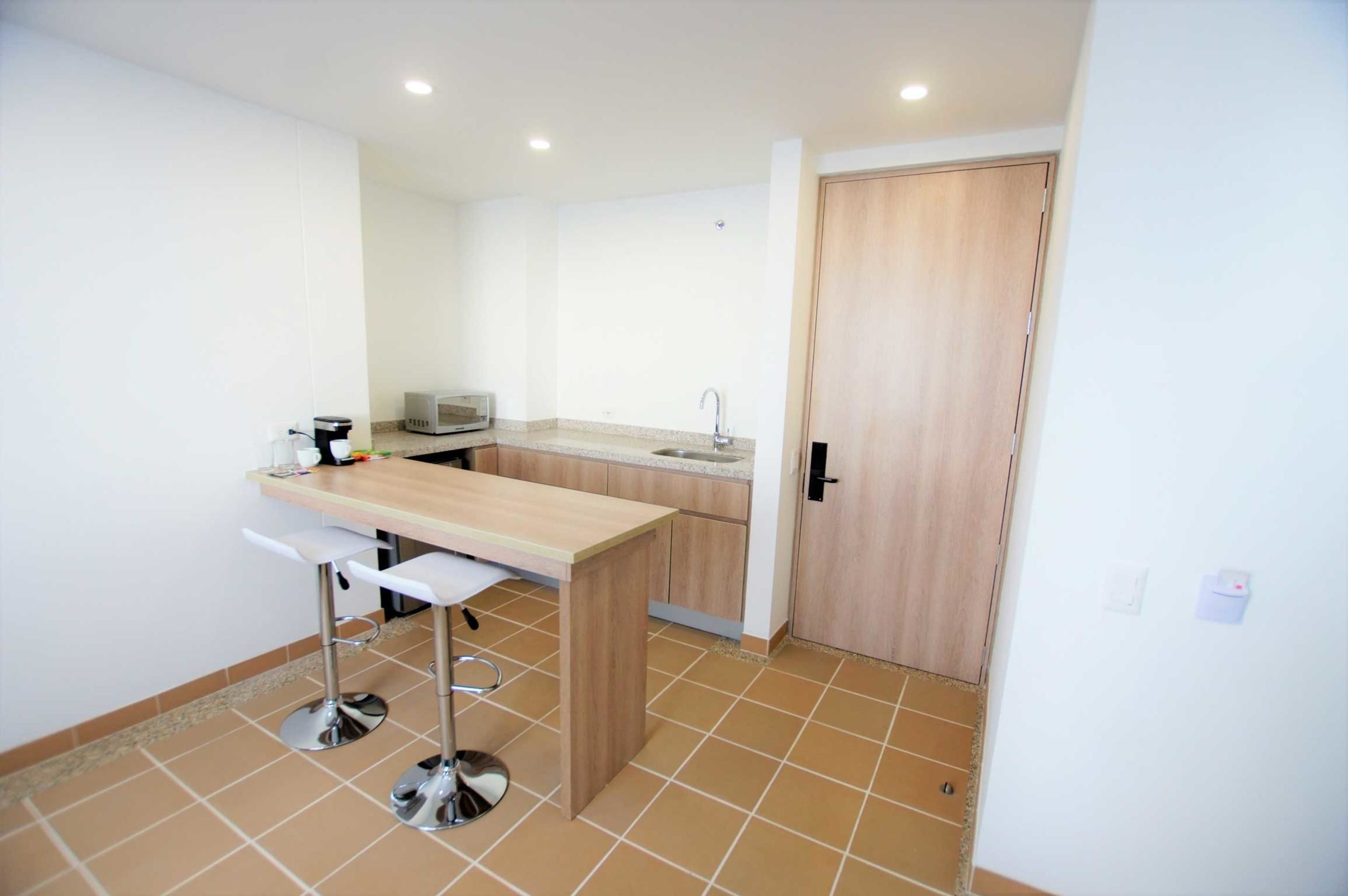 Cozinha compacta com bancada de madeira, dois bancos de bar brancos, micro-ondas e pia.