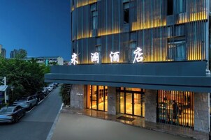 Um edifício moderno com sinalização iluminada, entrada coberta e área de estacionamento visível.