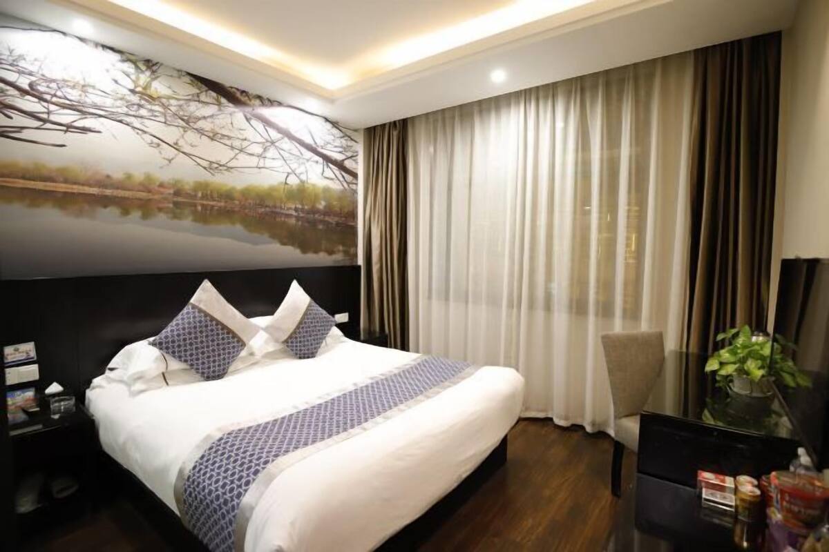 Quarto de hotel com uma cama grande, uma mesa de cabeceira, uma escrivaninha com uma planta e vista para um lago através de cortinas translúcidas.