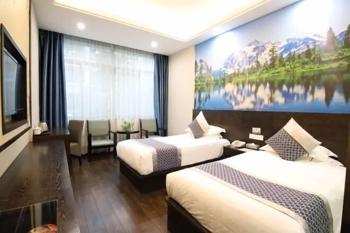 Quarto de hotel com duas camas, uma escrivaninha, uma cadeira, uma televisão e uma janela grande com cortinas.
