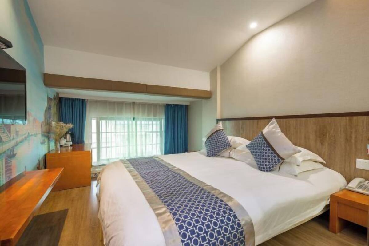 Quarto de hotel com uma cama grande, uma mesa, uma cadeira, um criado-mudo e uma janela com cortinas.