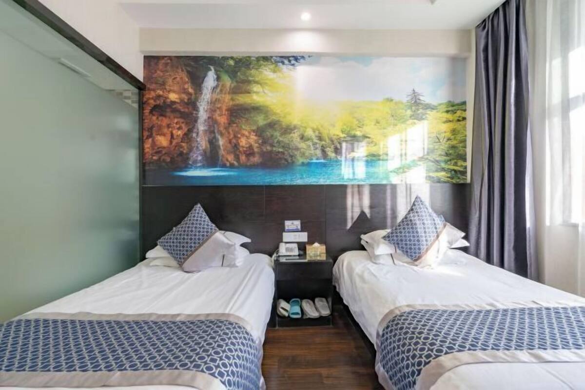 Quarto de hotel com duas camas, um grande mural na parede e uma mesa de cabeceira com chinelos.