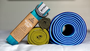 Um tapete de yoga, uma faixa de yoga enrolada e um bloco de yoga sobre uma superfície branca.