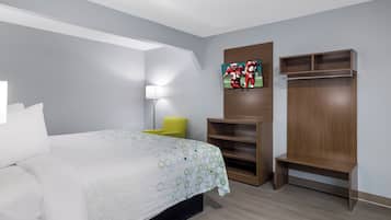 Quarto de hotel com uma cama, televisão fixada na parede, uma cadeira e um guarda-roupa de madeira.