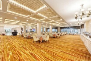 Um amplo hall de hotel com carpete estampado, diversas mesas de jantar e um design moderno no teto.