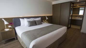Quarto de hotel moderno com uma cama grande, mesas de cabeceira, guarda-roupa e espelho.