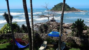 Um jardim costeiro com uma rede, cadeiras de descanso e um guarda-sol azul.