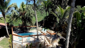 Uma área de piscina com deck de pedra, palmeiras e deck de madeira com vista para a piscina.