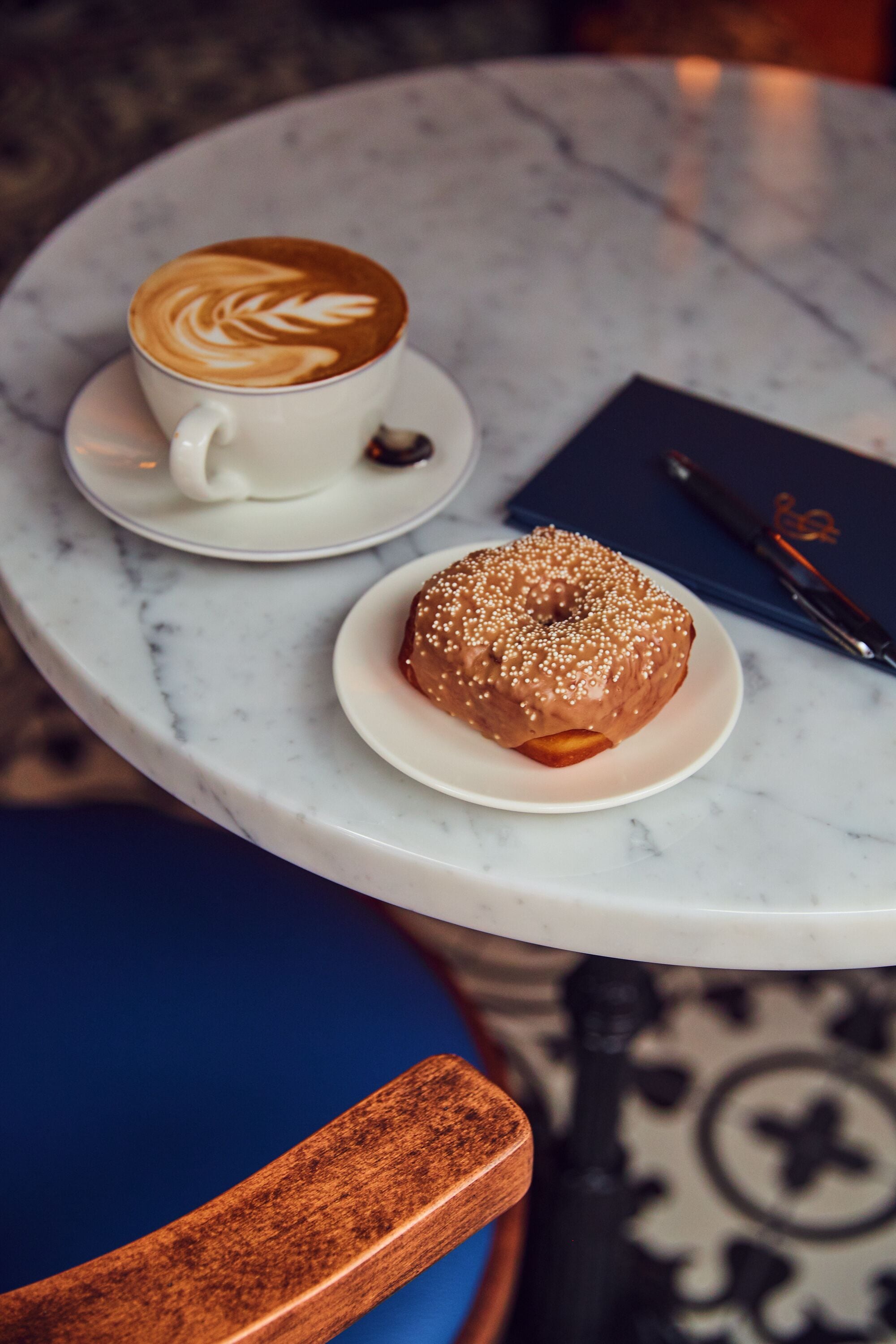 Uma mesa redonda de mármore com uma chávena de café, um donut e um caderno.