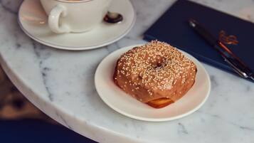 Uma mesa redonda de mármore com uma chávena de café, um donut e um caderno.