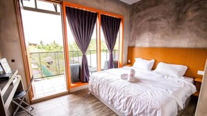 Quarto com cama grande, escrivaninha e vista para uma varanda.