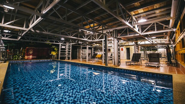Piscina interior com piso azulejado e teto alto com vigas de metal.